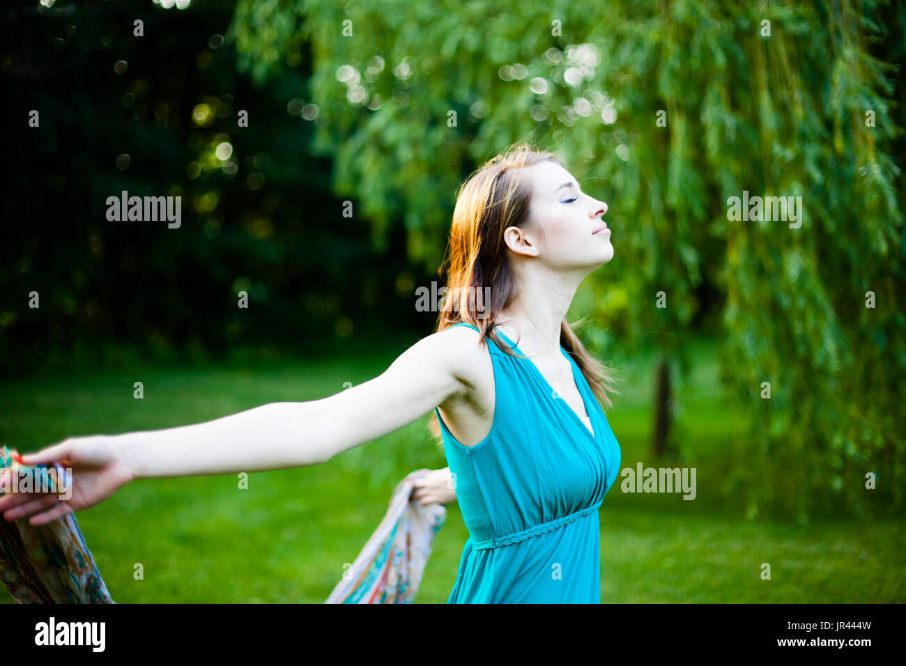 Beautiful girl is slowly spinning around in front of a willow tree ...