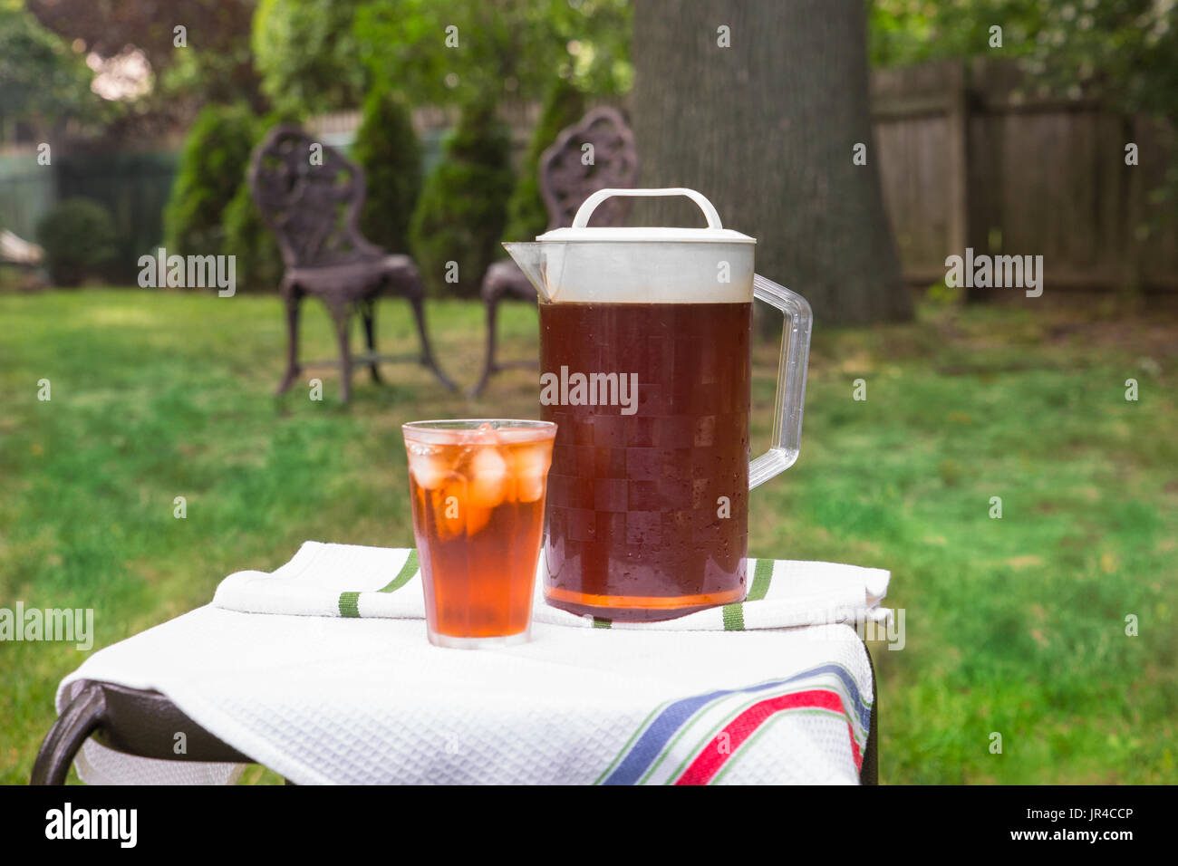 Pitcher of iced tea and a glass in outdoor backyard summer setting ...