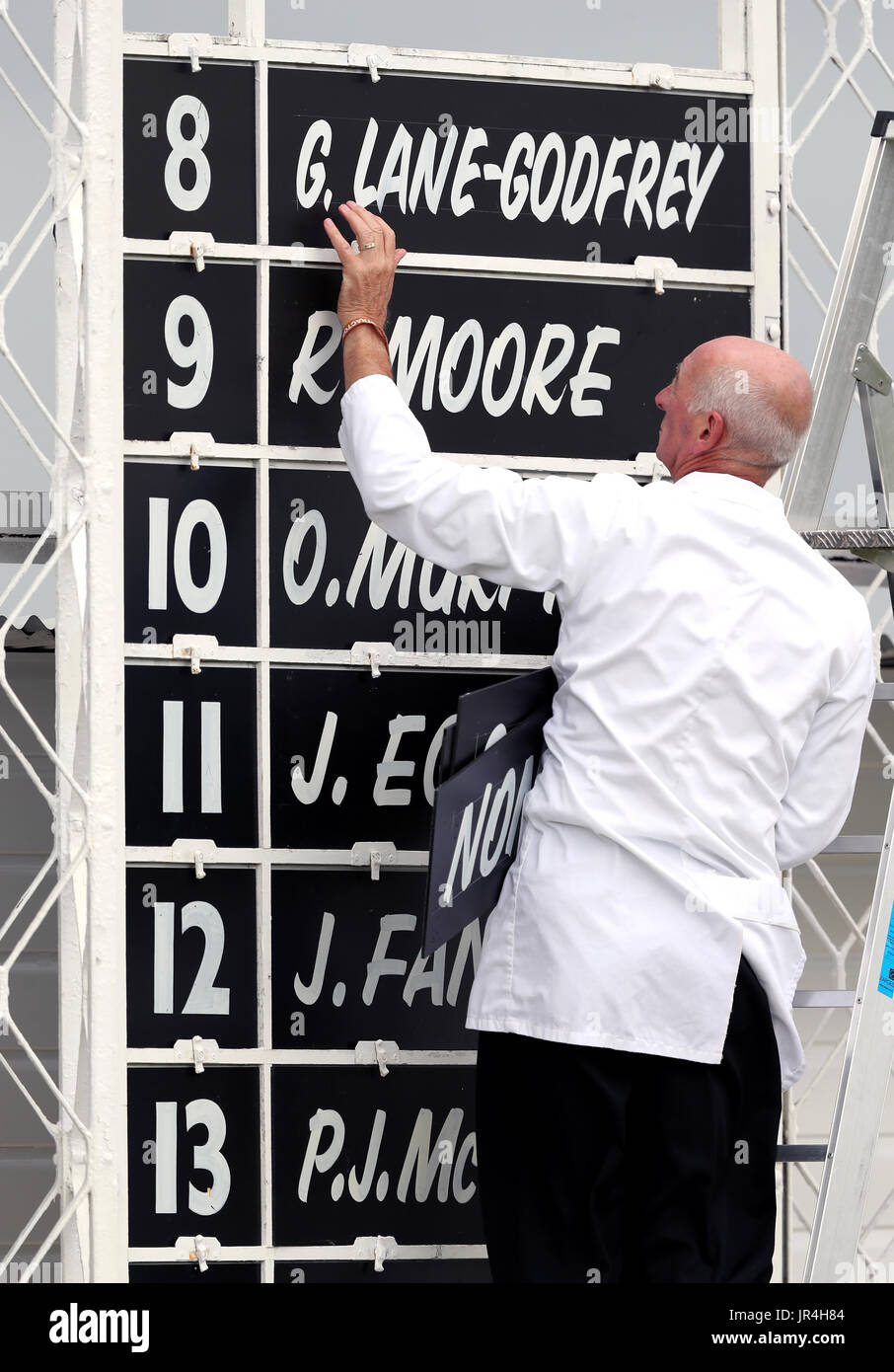 A member of the course staff changes the jockey names on a riders board ...