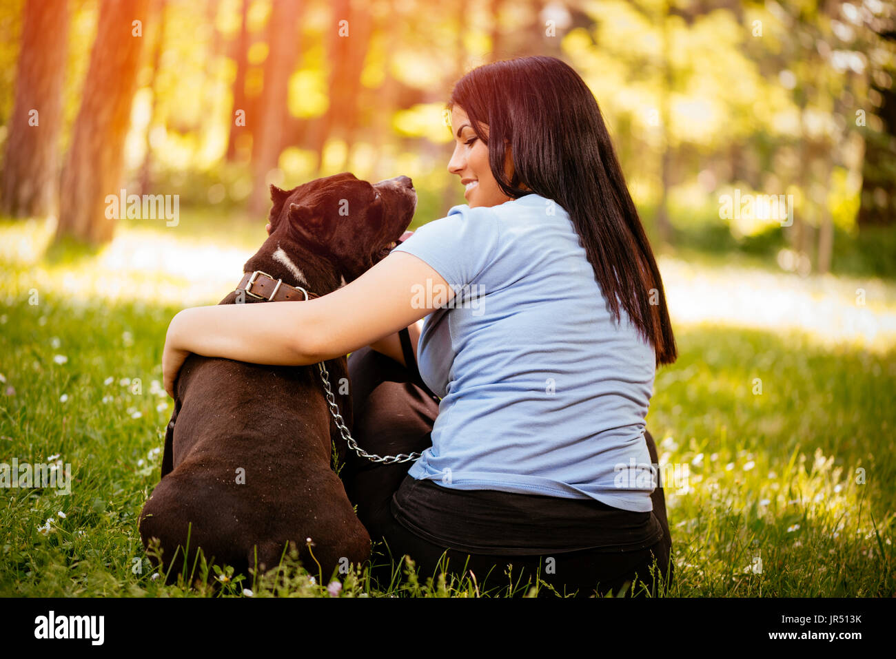 Rear view of a beautiful young woman hugging her cute stafford terrier ...