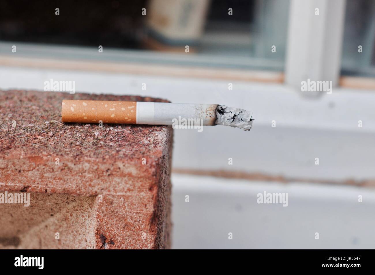 Burning cigarette on the brown brick near window. Cigarette addict ...