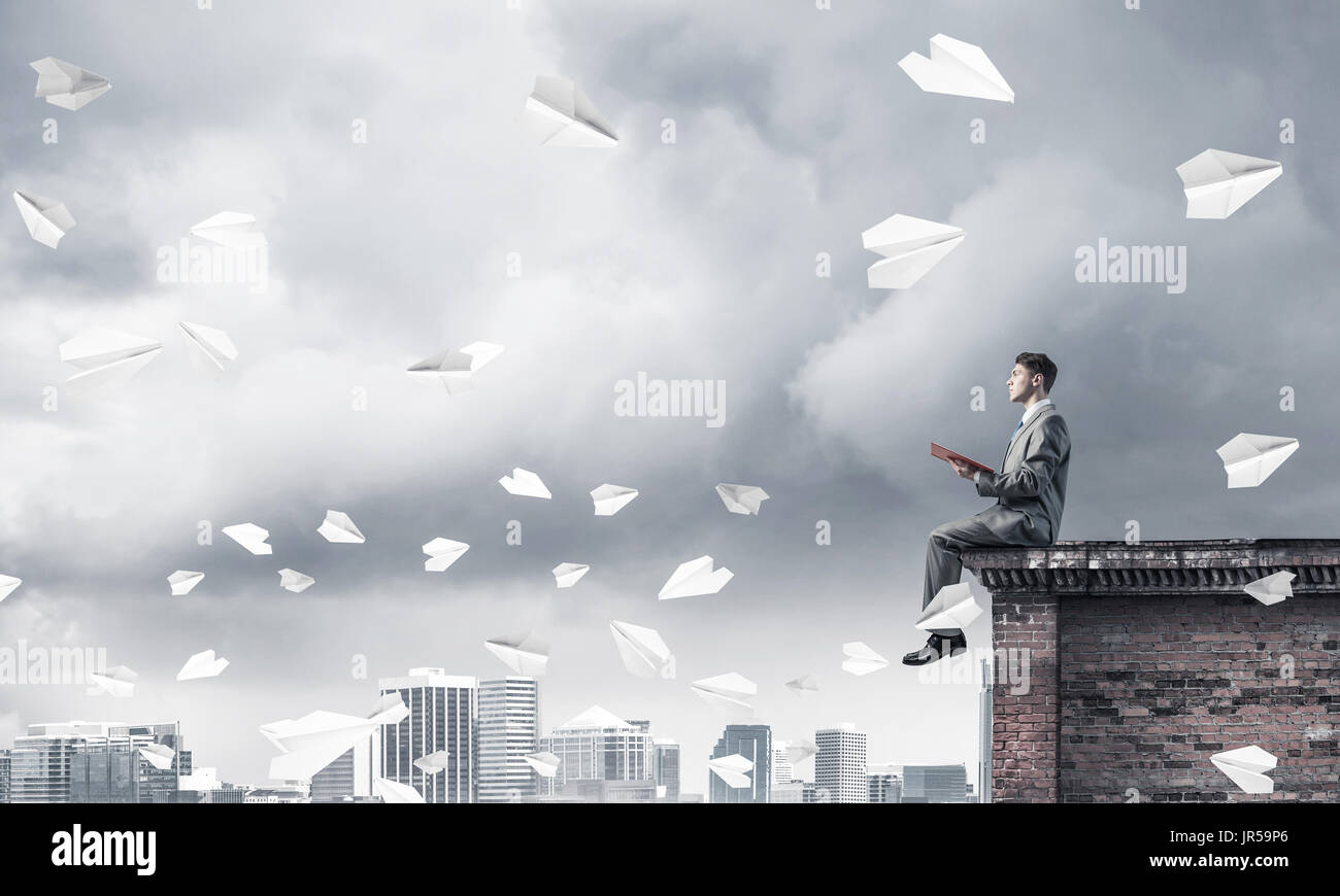 Man on roof edge reading book and cityscape at background Stock Photo ...