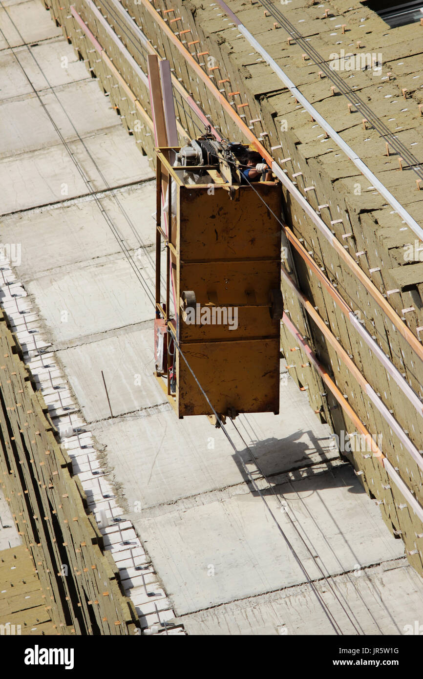 worker in yellow suspended cradle mounts environmental boards for ...