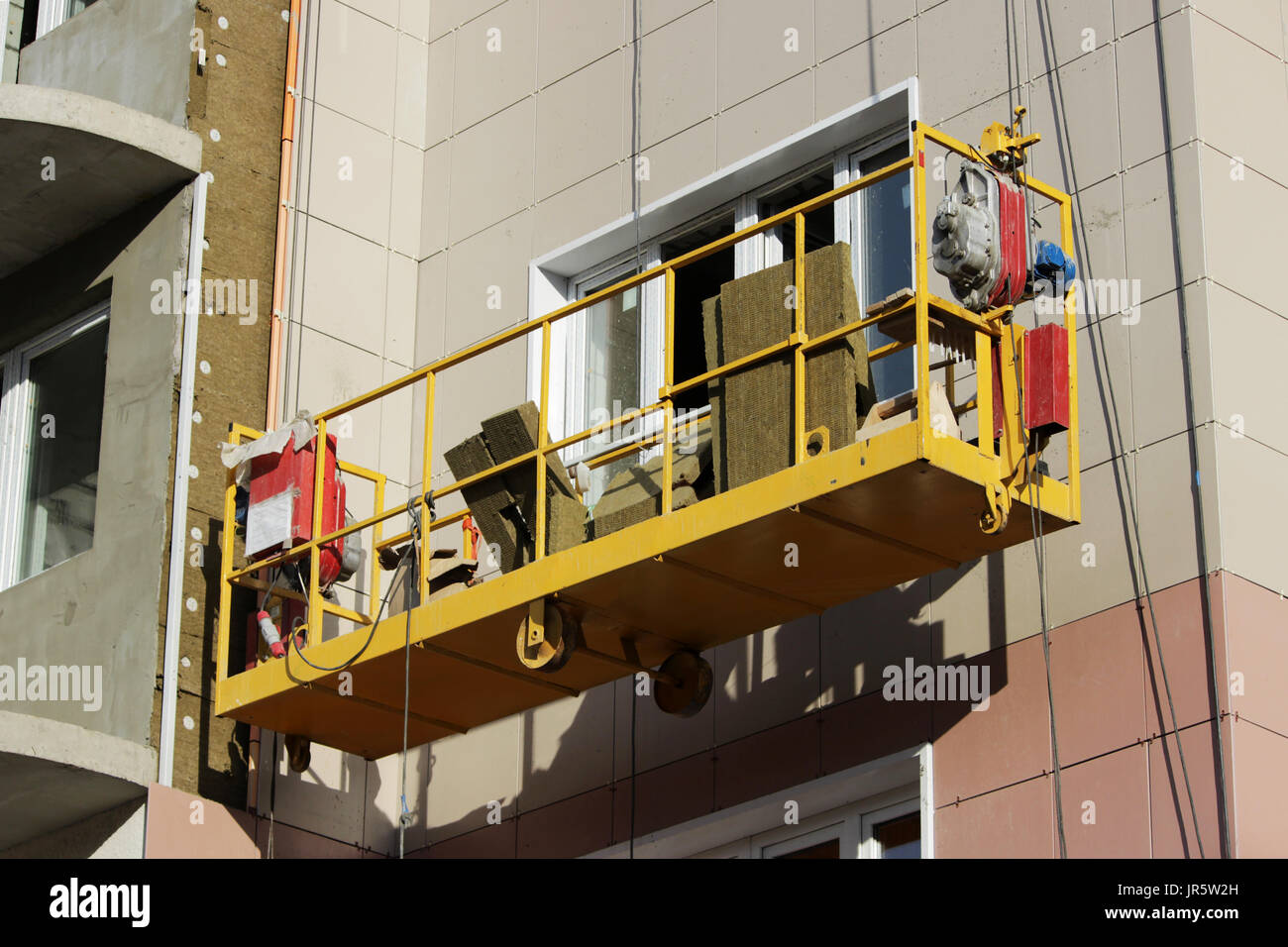 worker in yellow suspended cradle mounts environmental boards for ...