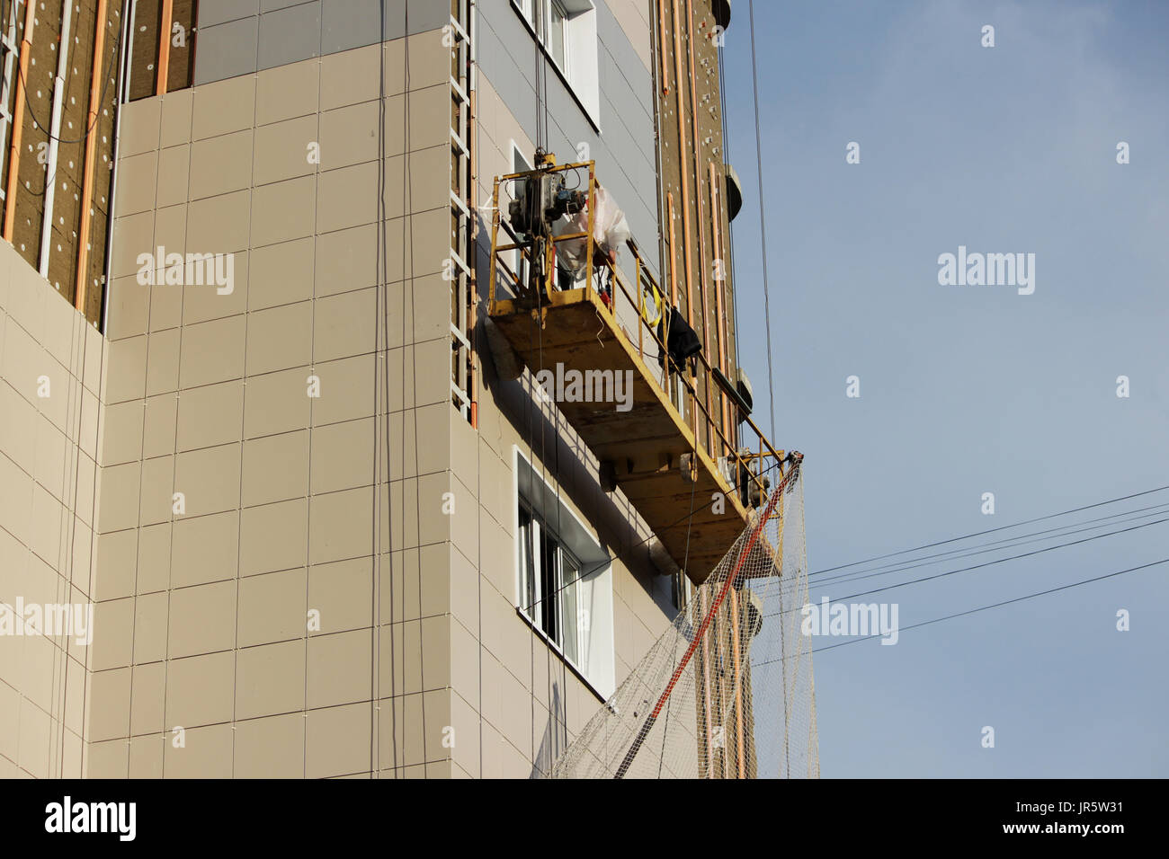 worker in yellow suspended cradle mounts environmental boards for ...