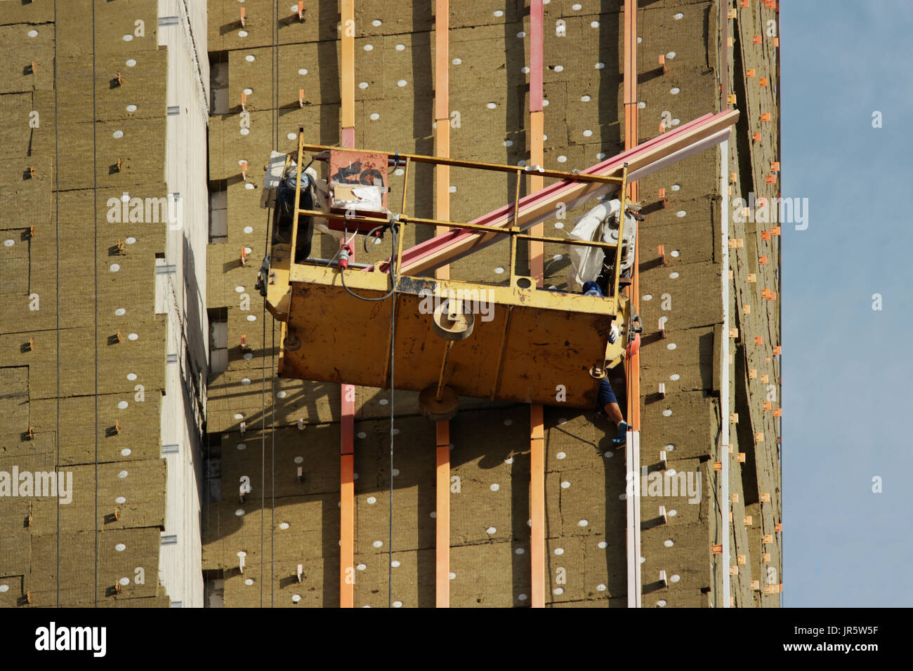 worker in yellow suspended cradle mounts environmental boards for ...