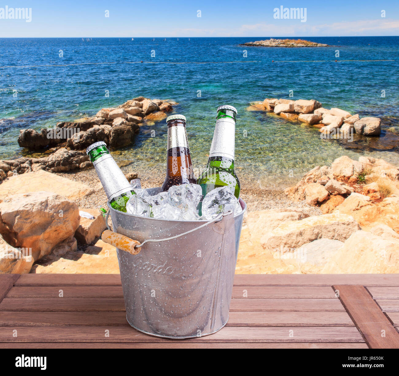 Three unopened bottles of beer inside ice bucket on beach background ...