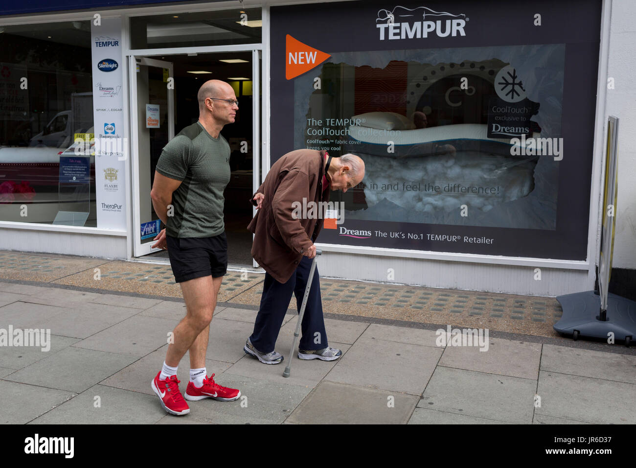 A very muscular, fit and upright man walks alongside a stooping elderly ...