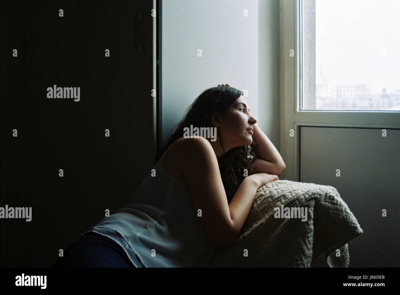 Woman sitting on a chair looking through a window Stock Photo - Alamy