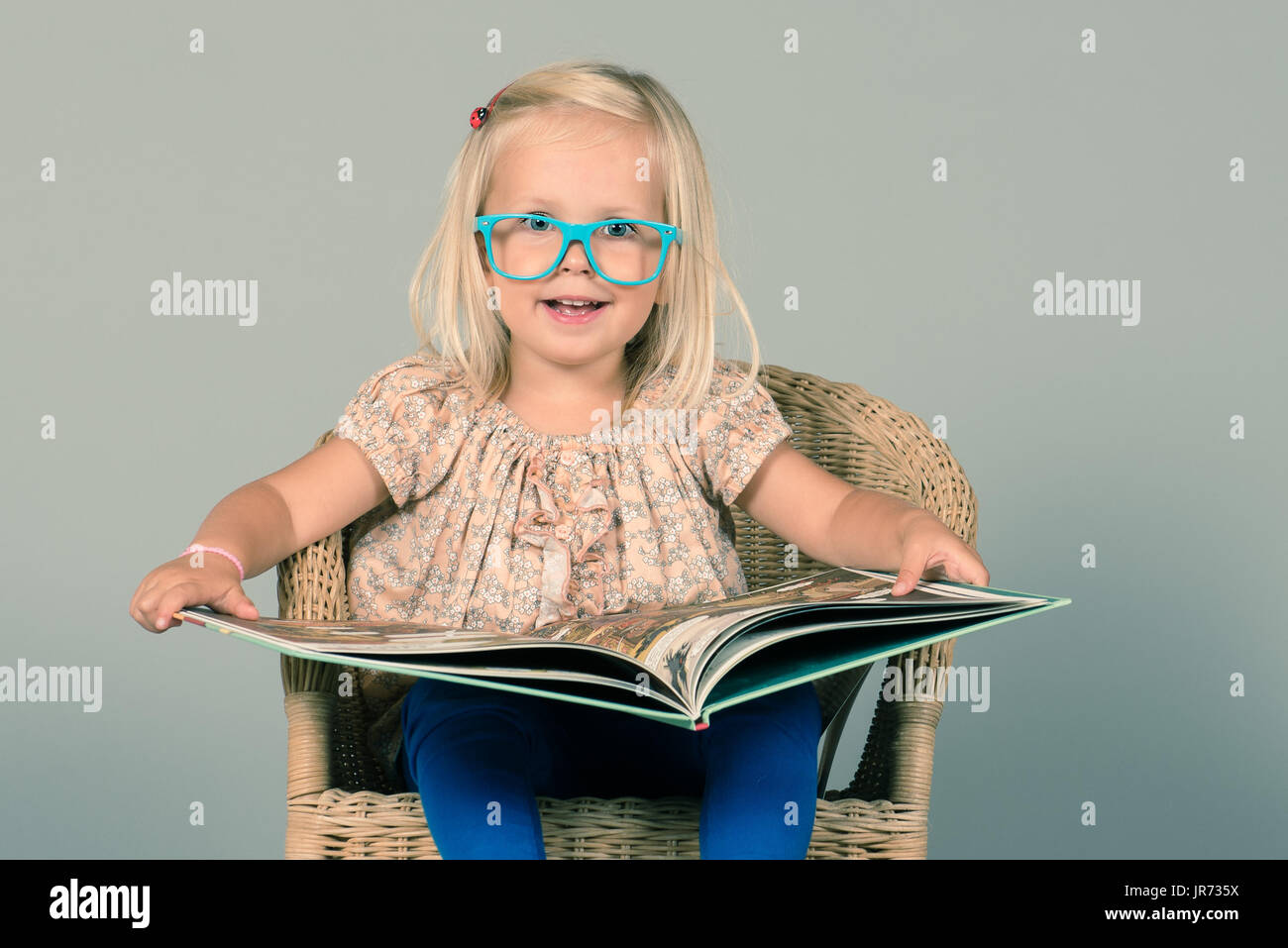Cute little girl siting on the chair and reading big book with ...