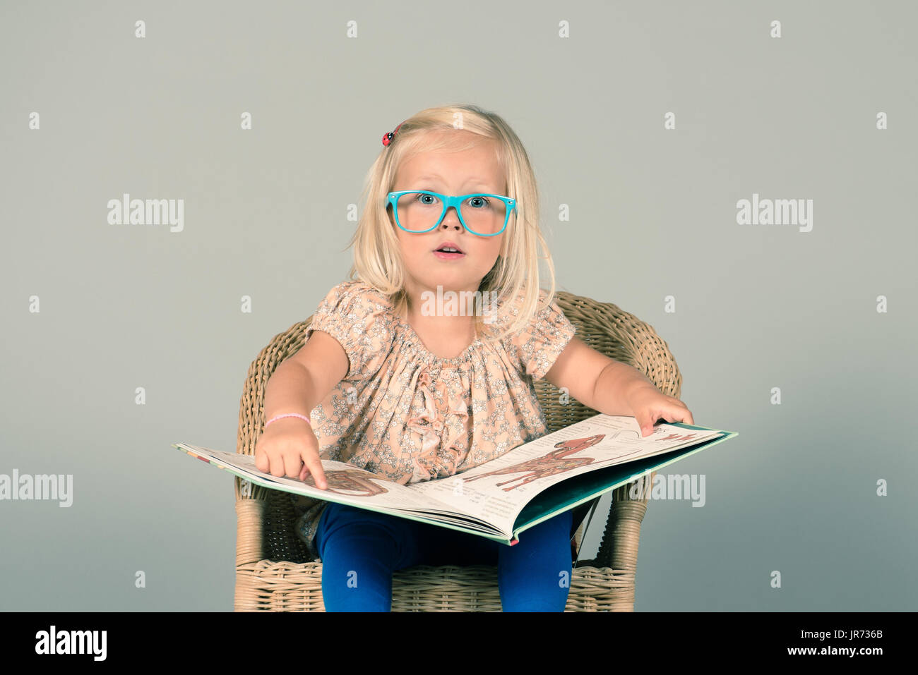 Cute little girl siting on the chair and reading big book with ...