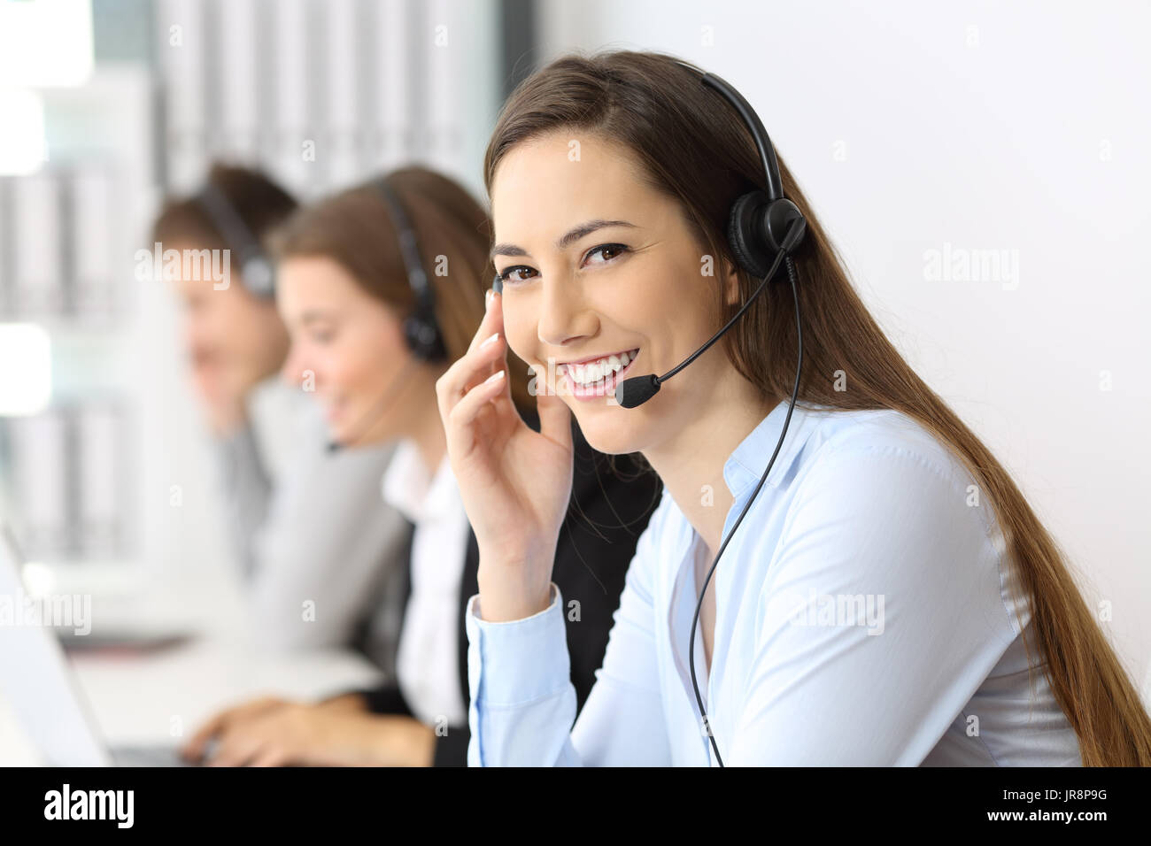 Happy telemarketer looking at you at office with other workers in the ...