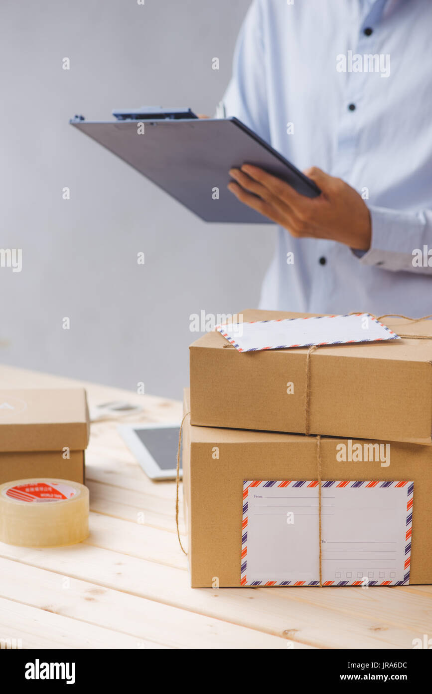 Courier making notes in delivery receipt among parcels at table Stock ...