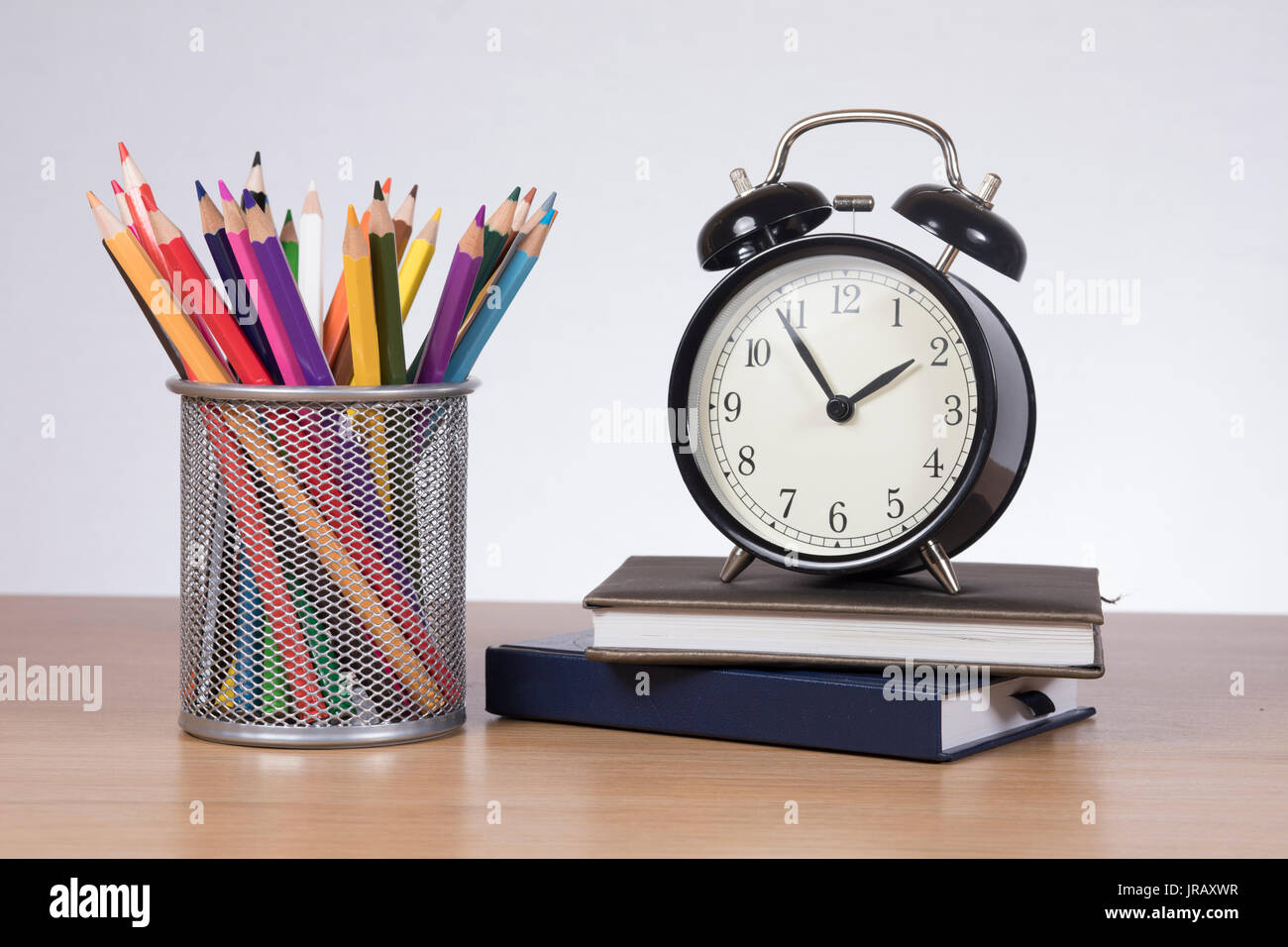 Colored pencils in holder standing by notebooks with alarm clock Stock ...