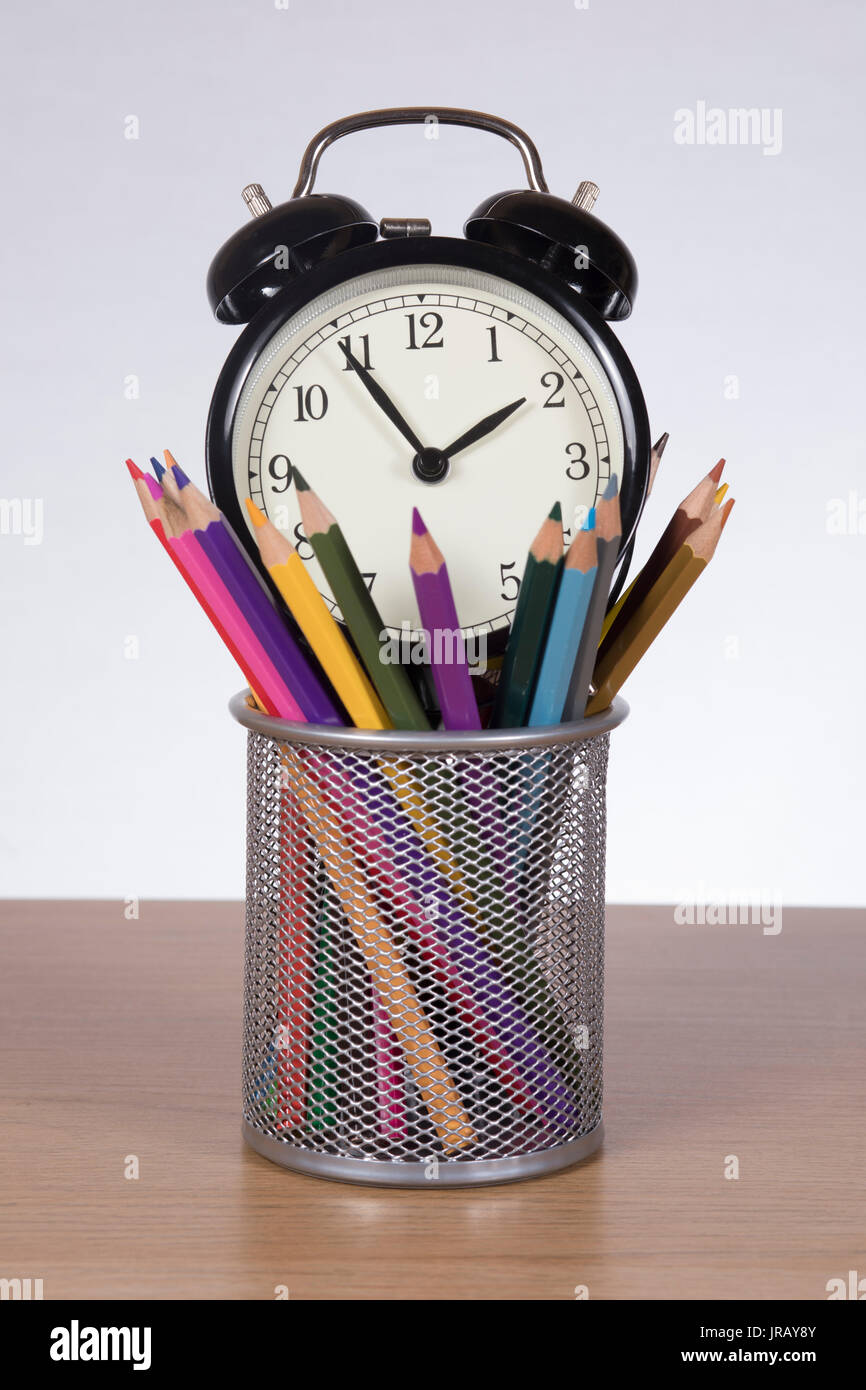 Alarm clock put into container with colored pencils standing on wooden ...