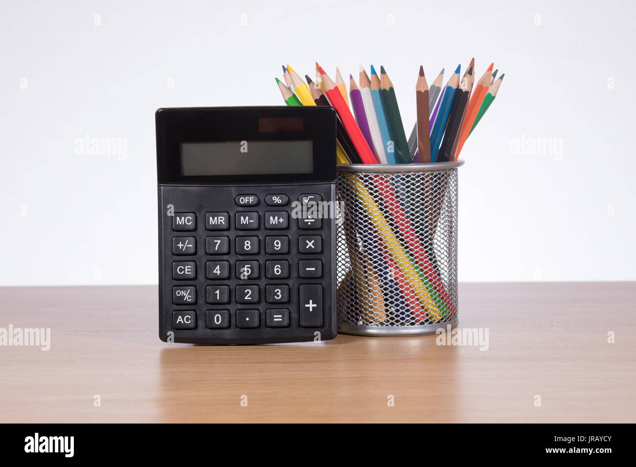 Calculator with colored pencils in container standing on desk Stock ...