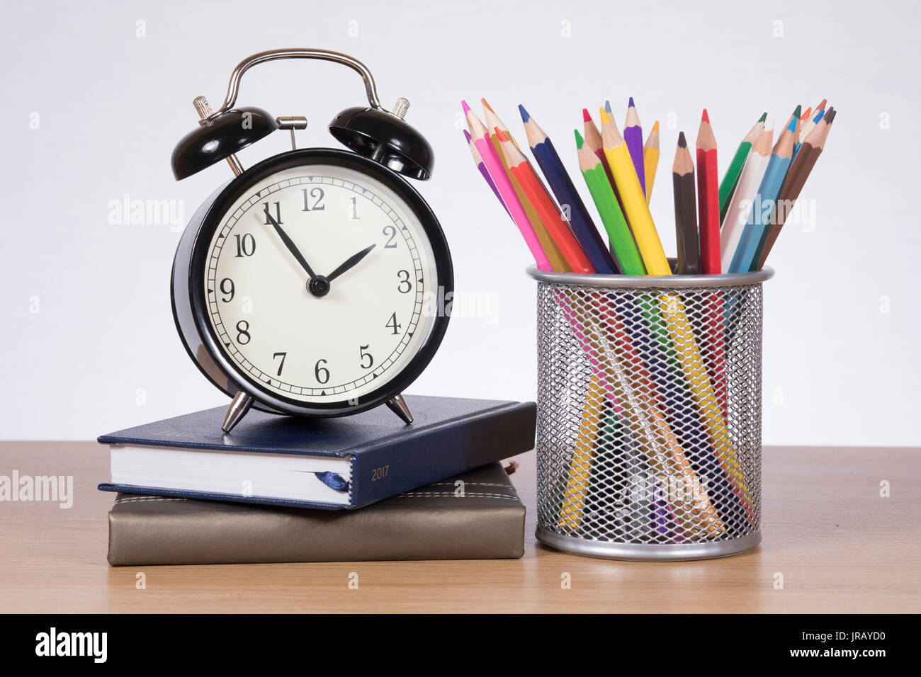 Stacked books with an alarm clock and coloured pencils on a timber desk ...