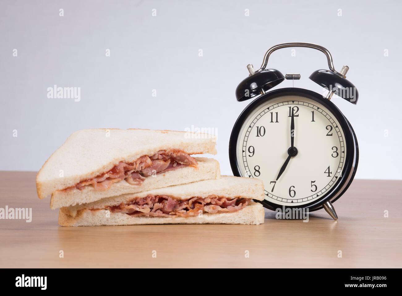Fresh homemade bacon or meat sandwich and alarm clock with the time ...