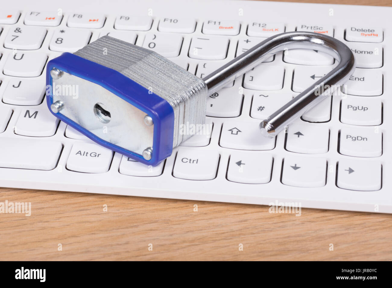 Open steel padlock lying on a white computer keyboard in a low angle ...