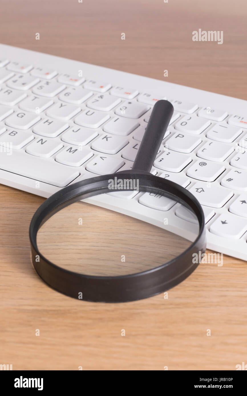 Black magnifying glass laying over white computer keyboard on the desk ...