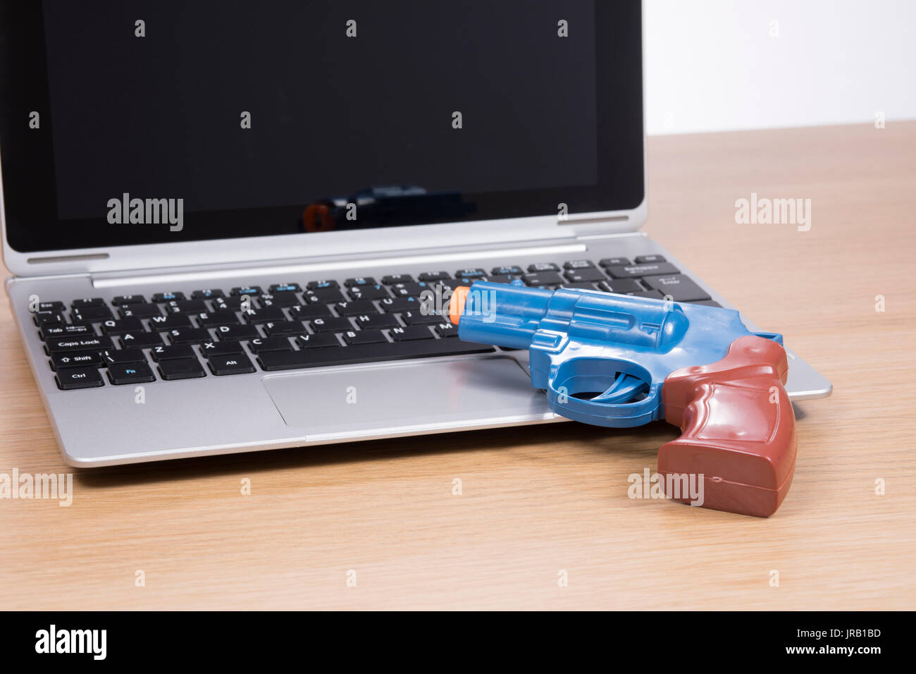 Open laptop with small toy gun lying on the keyboard on a wooden desk ...