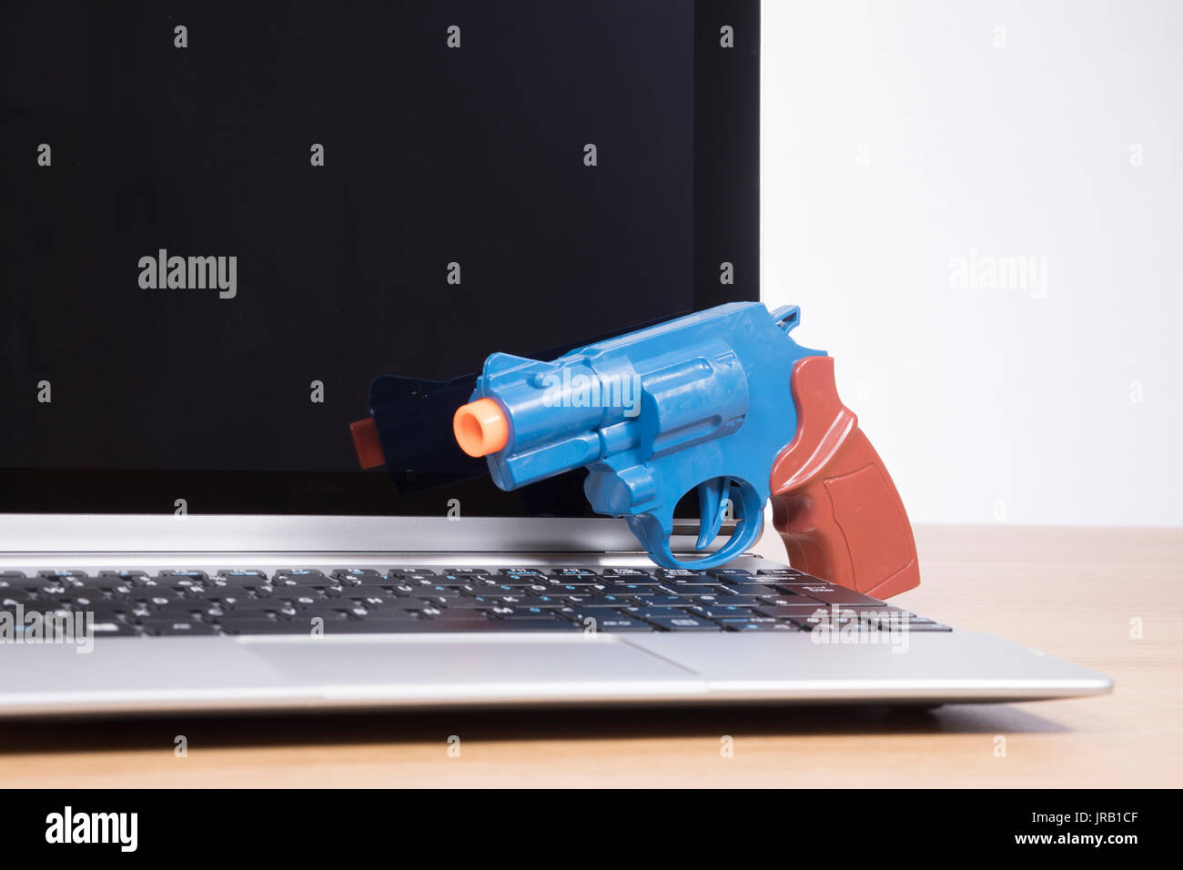 Open laptop with toy pistol standing on desk against plain background ...