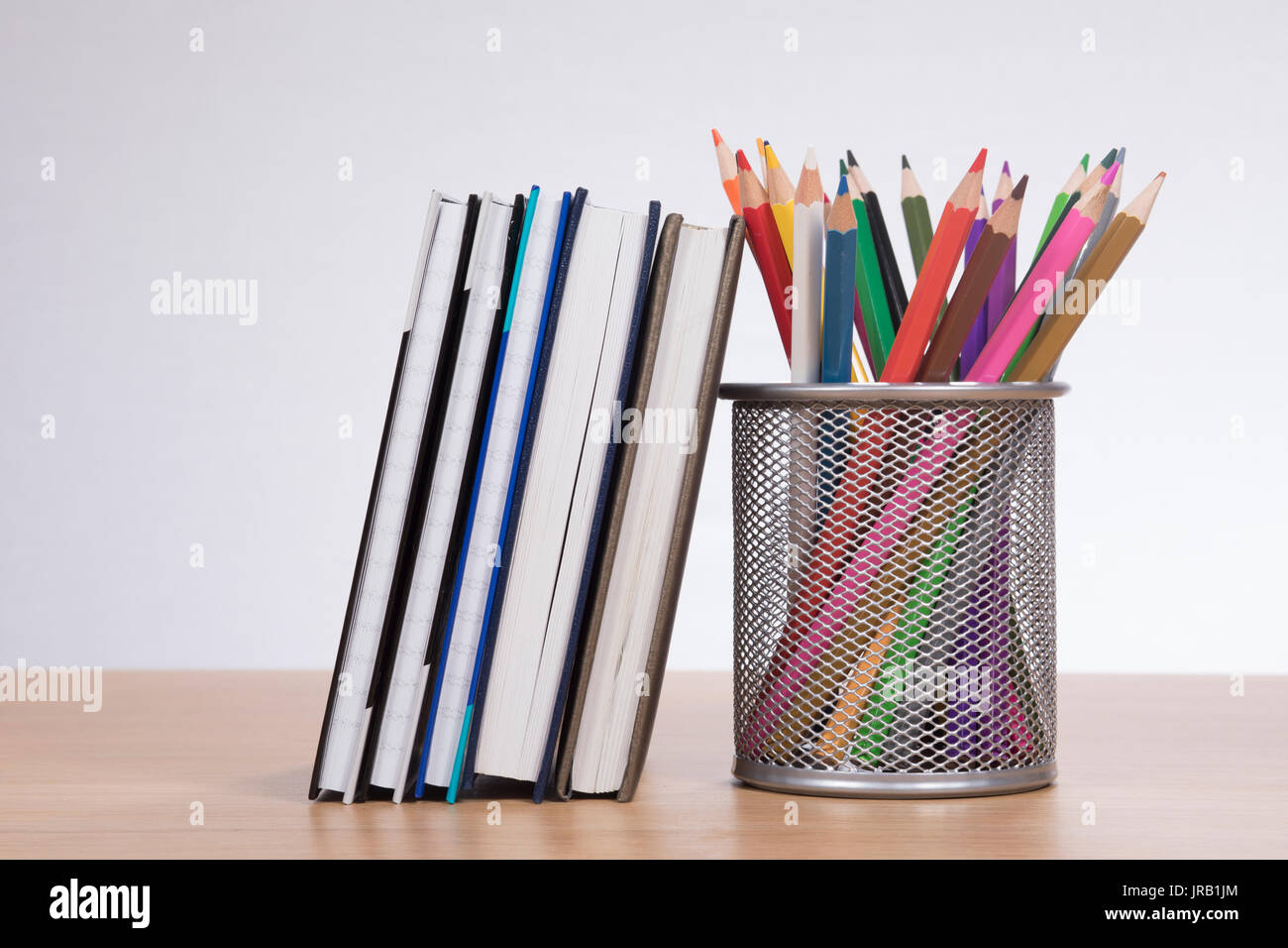 School books with a set of colored pencil crayons in a wire mesh ...