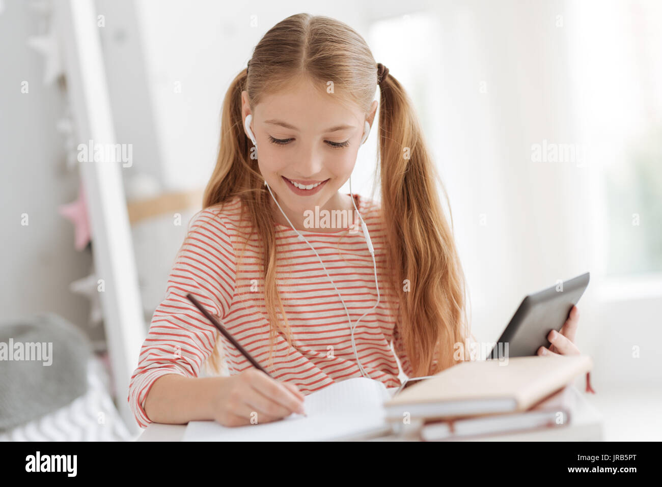 Diligent female pupil doing homework and listening music Stock Photo ...