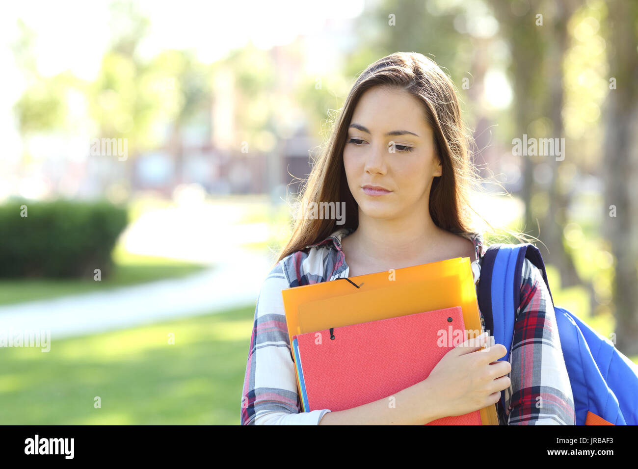 Front view portrait of a sad student walking in the street holding ...