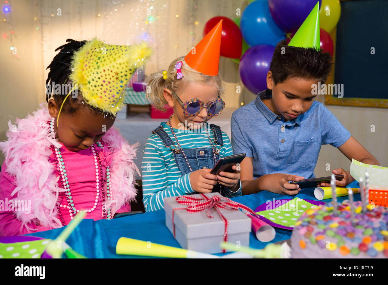 Children using mobile phone while sitting at table during birthday ...