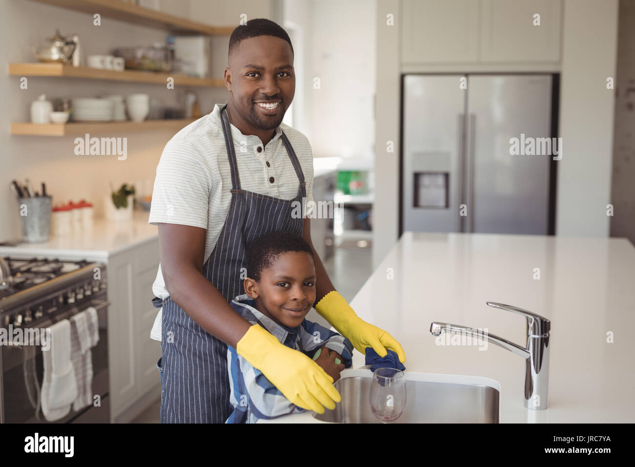 Portrait of smiling father and son cleaning wine glass in kitchen at ...