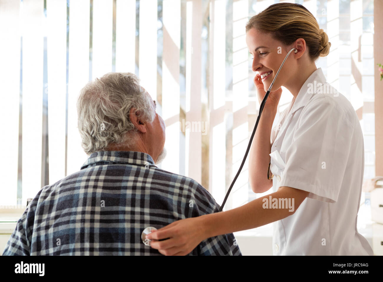 Female doctor examining senior patient with stethoscope at nursing home ...