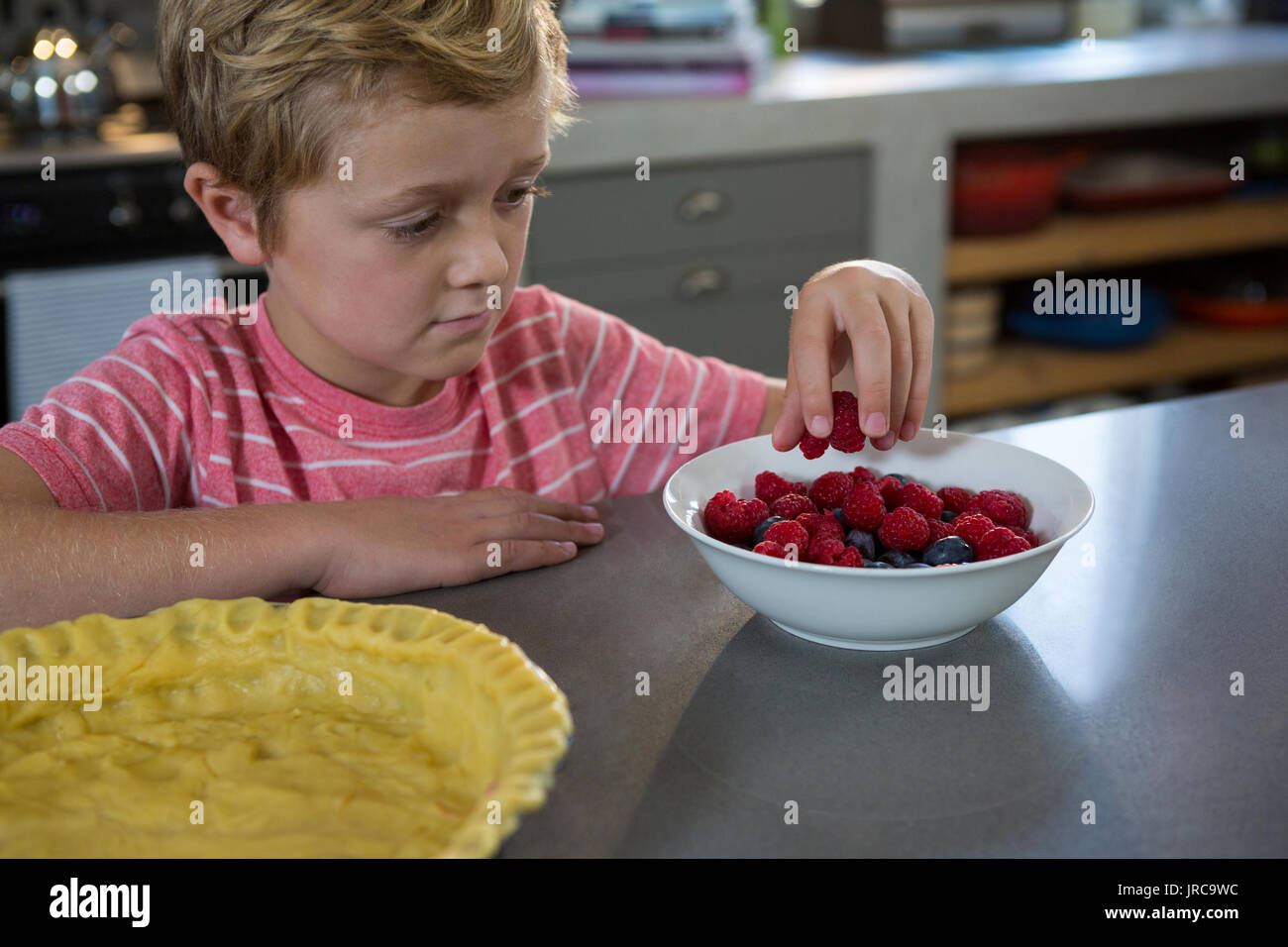 Boy having raspberries at kitchen counter Stock Photo - Alamy