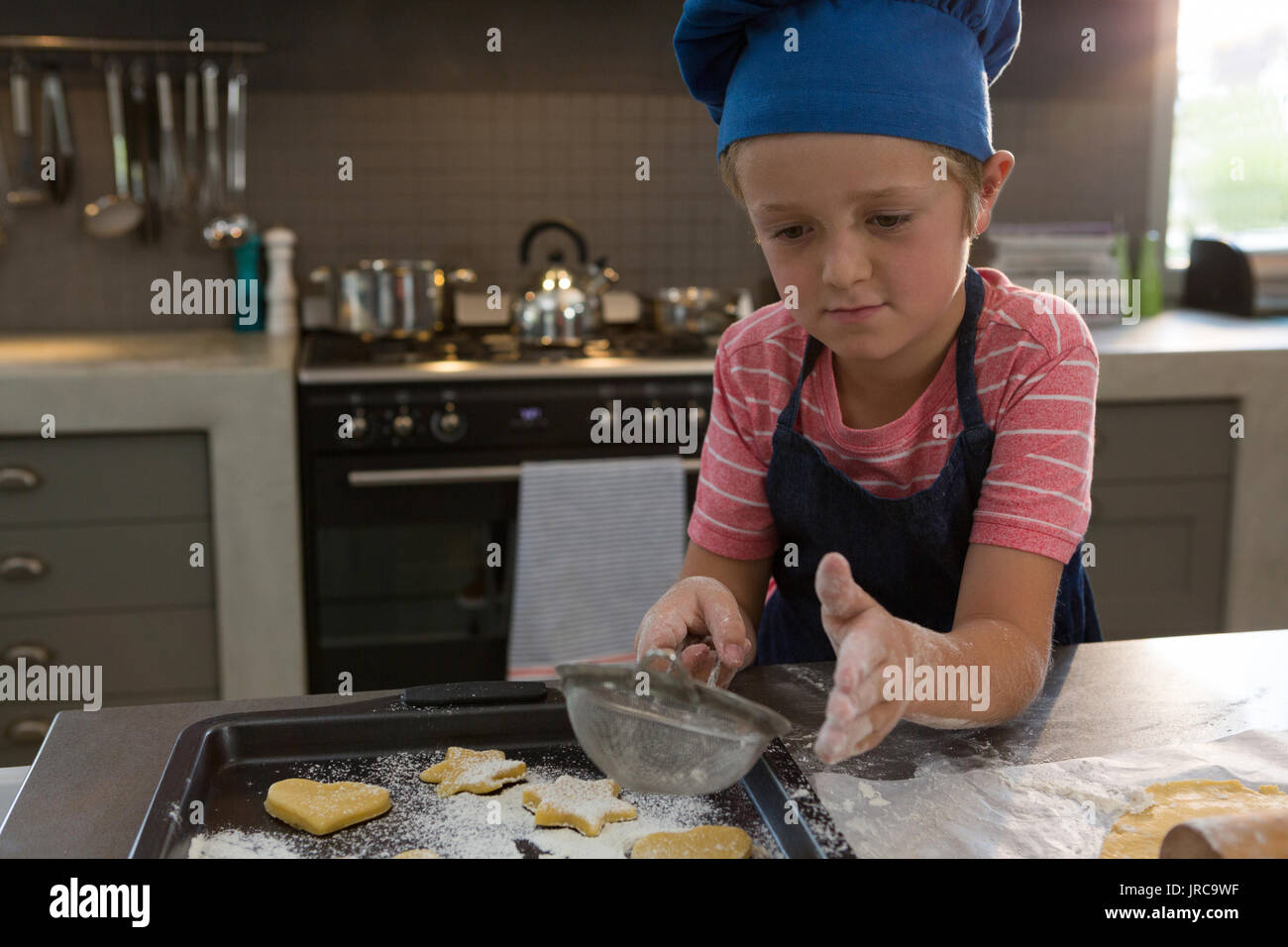 Boy sprinkling flour on cookies at kitchen counter Stock Photo - Alamy