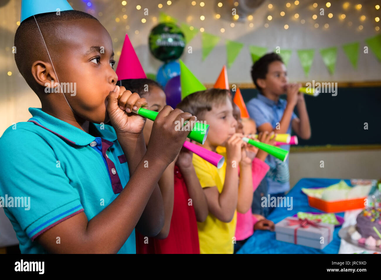 Children blowing party horns while standing by table during birthday ...