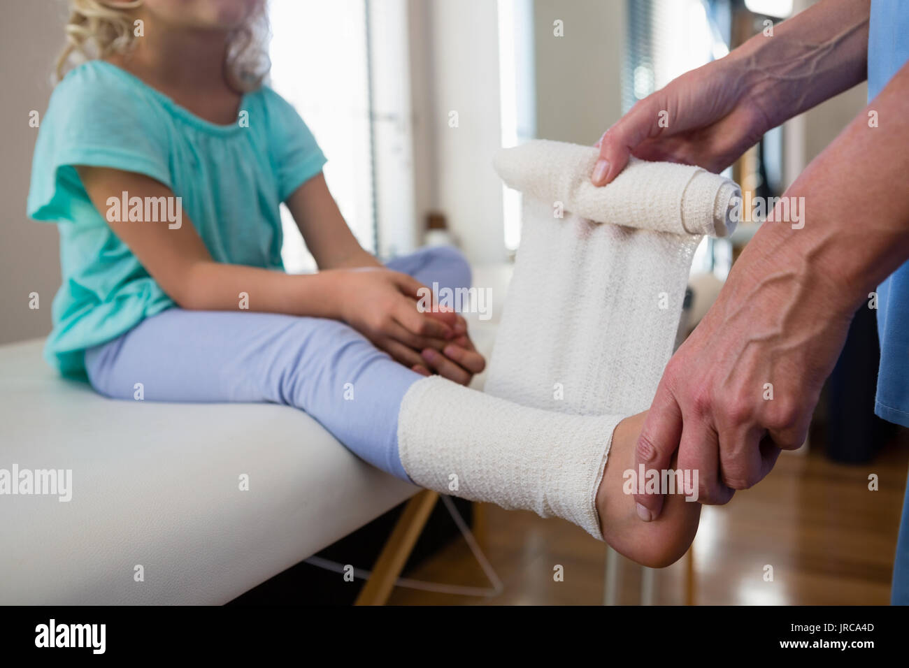Physiotherapist putting bandage on injured feet of girl patient in ...