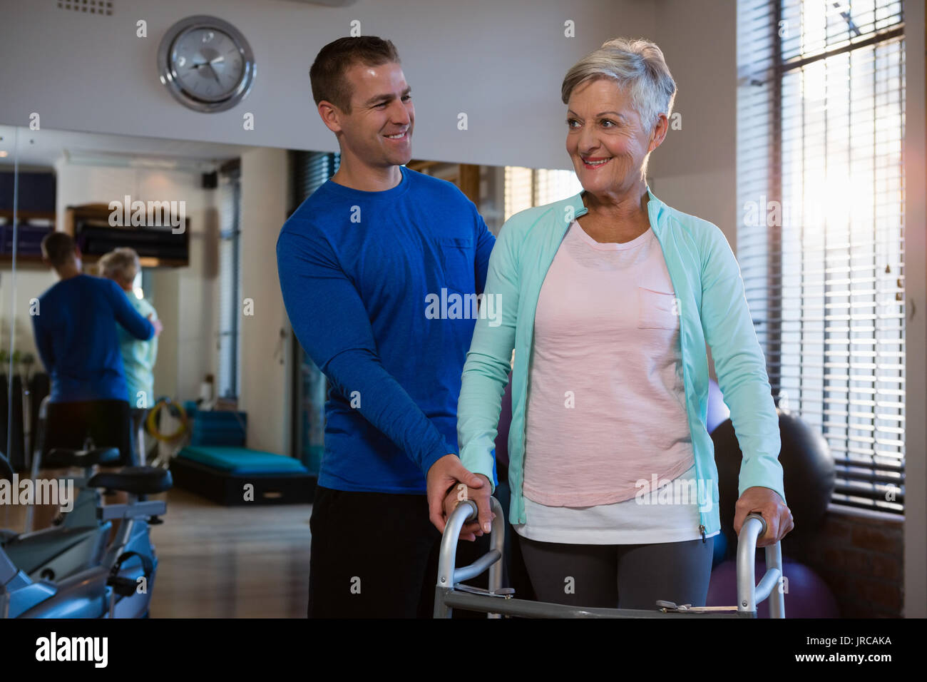 Physiotherapist assisting senior patient to walk with walking frame in ...