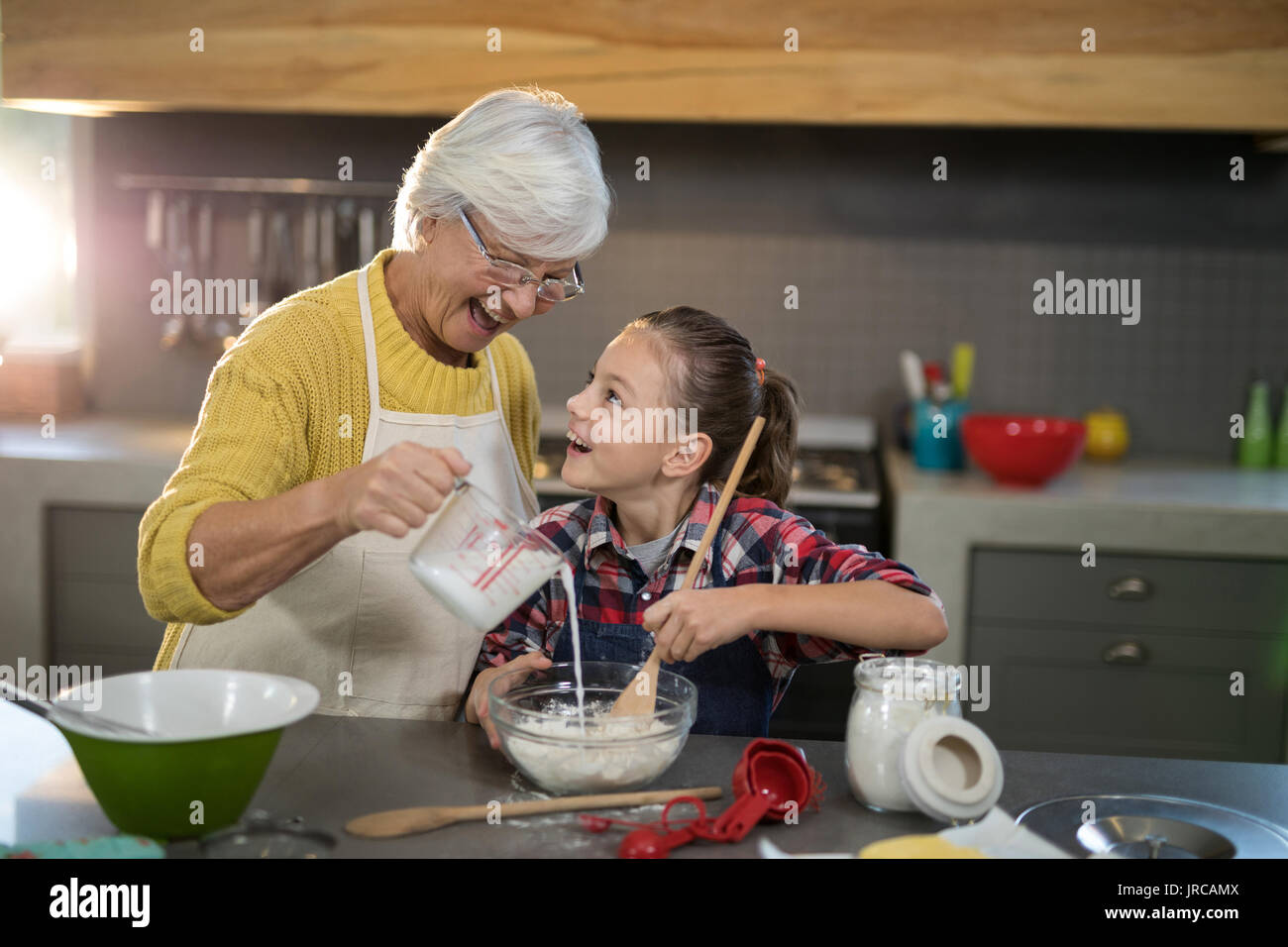 Grandmother adding water while granddaughter is mixing flour in a bowl ...