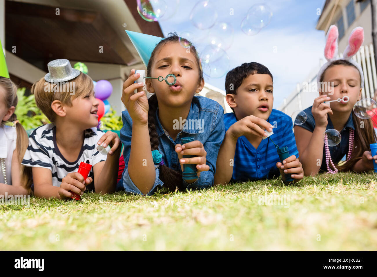 Children blowing bubbles while lying on field in yard Stock Photo - Alamy