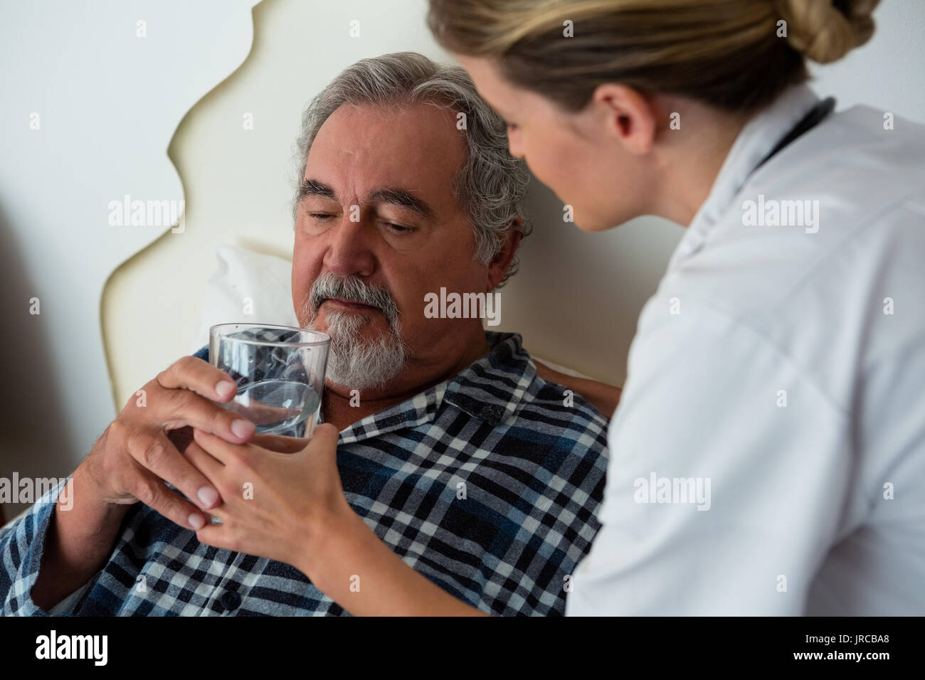Side view of female doctor giving water to senior patient in nursing ...