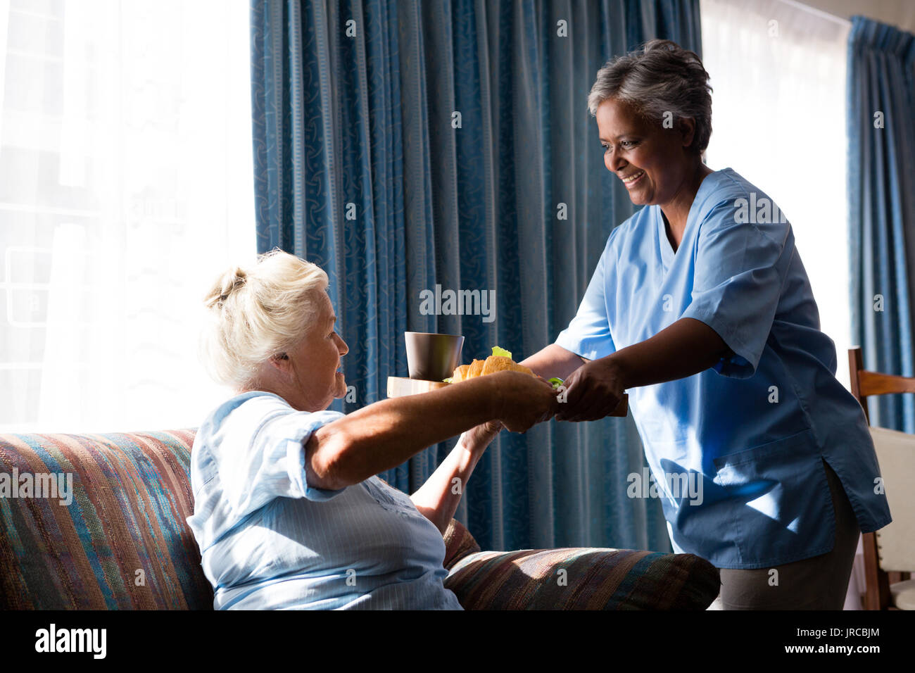 Doctor serving food to senior woman sitting on sofa in nursing home ...
