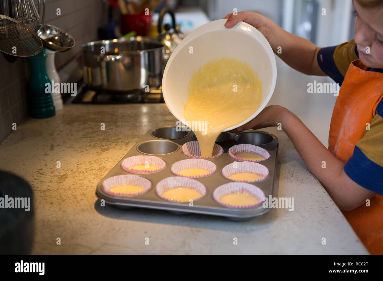 Boy pouring batter in cupcake holders at kitchen counter Stock Photo ...