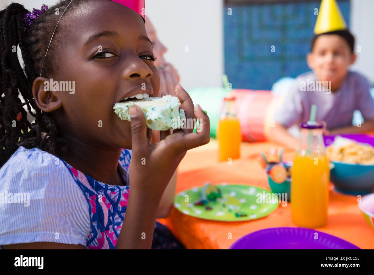Portrait of girl eating cake with friends in background during birthday ...