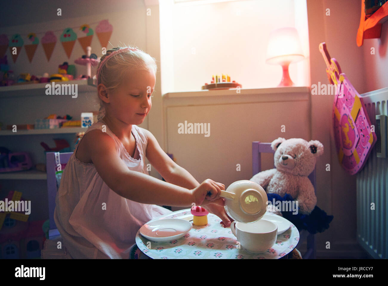 Little girl playing tea-party serving a cup of tea for toy bear ...