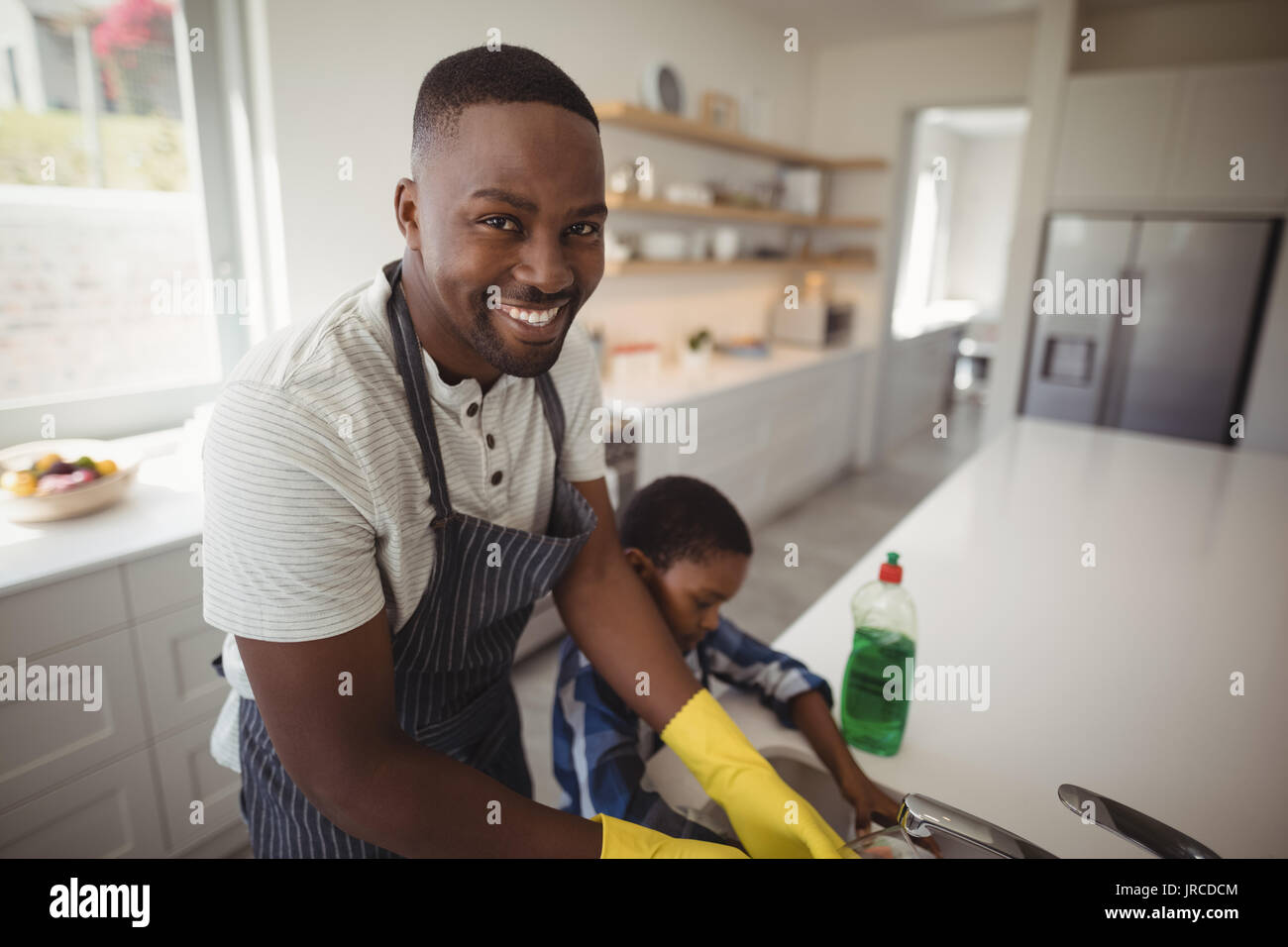 Portrait of smiling father and son cleaning utensils in kitchen at home ...