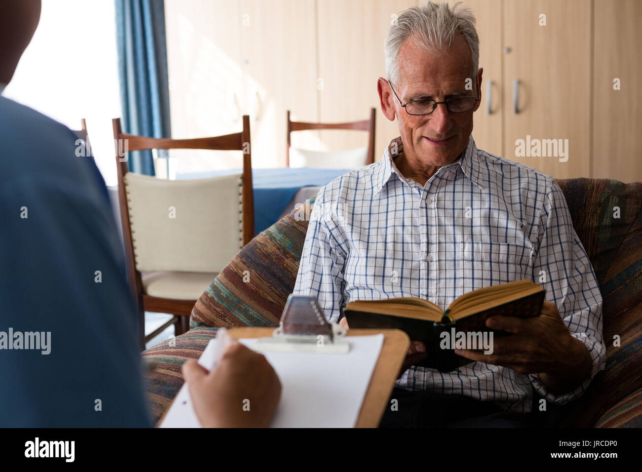 Female doctor writing on paper while senior man reading book in nursing ...