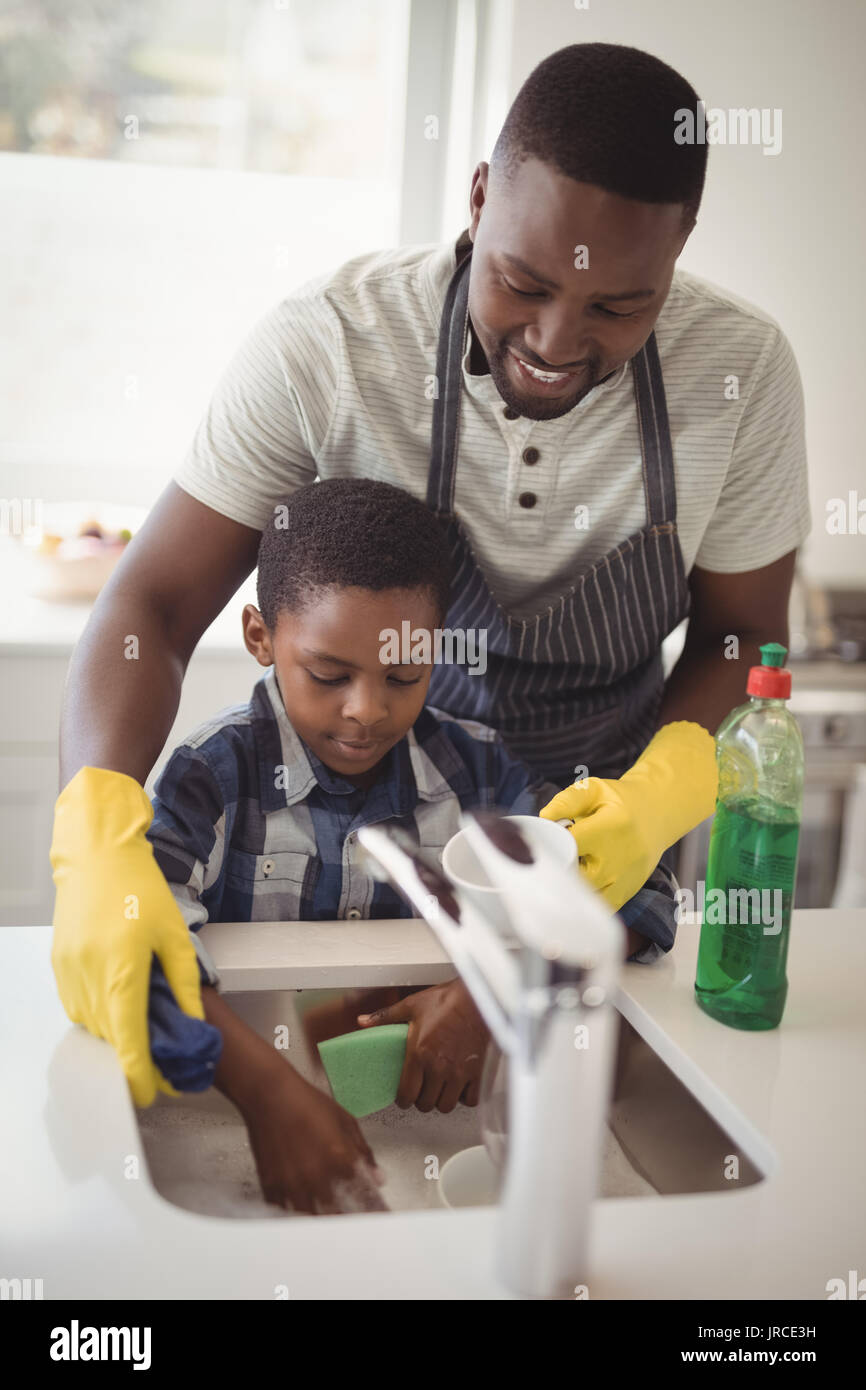 Smiling father and son cleaning utensils in kitchen at home Stock Photo ...