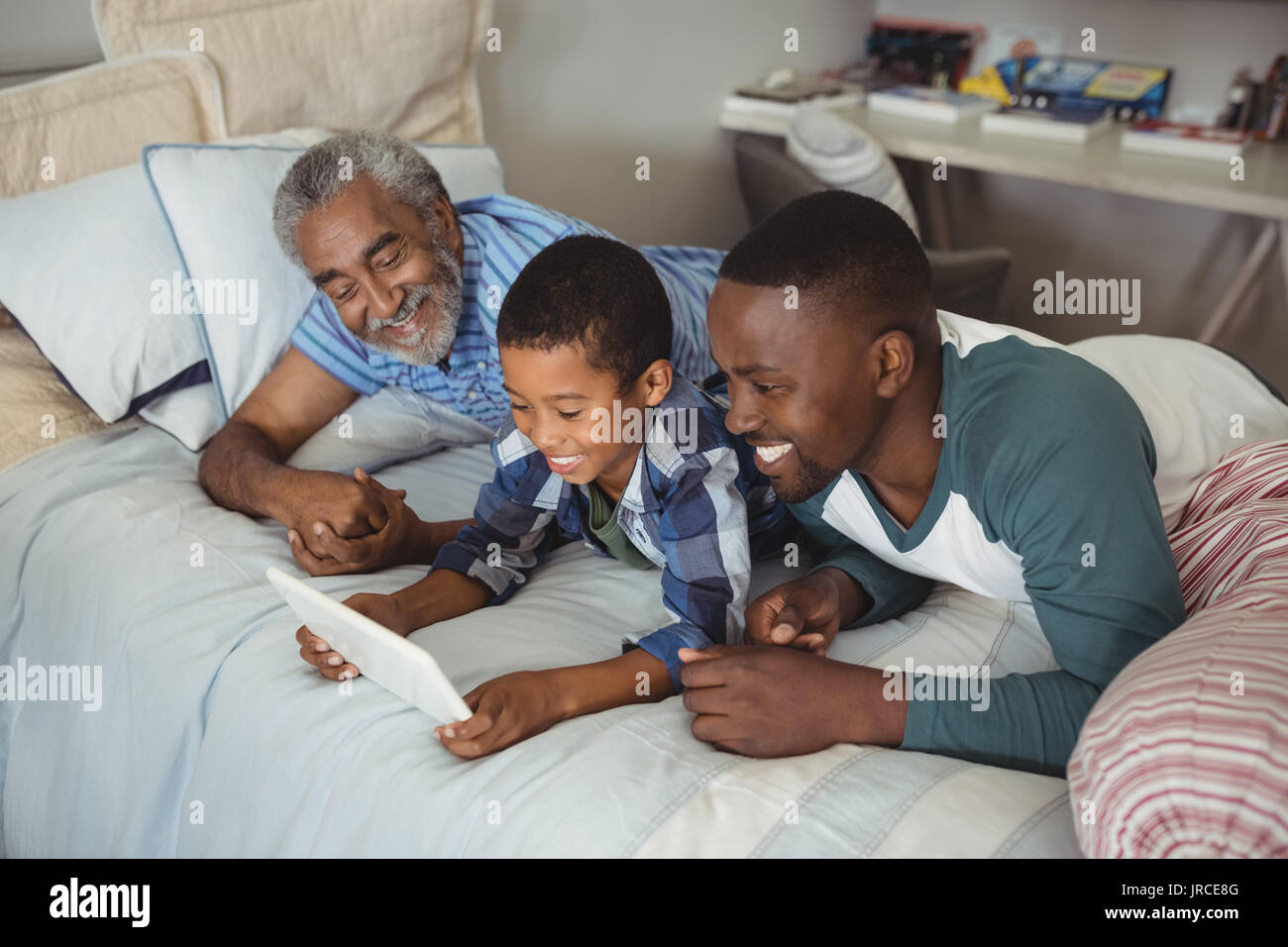 Happy multi-generation family using digital tablet on bed in bedroom ...