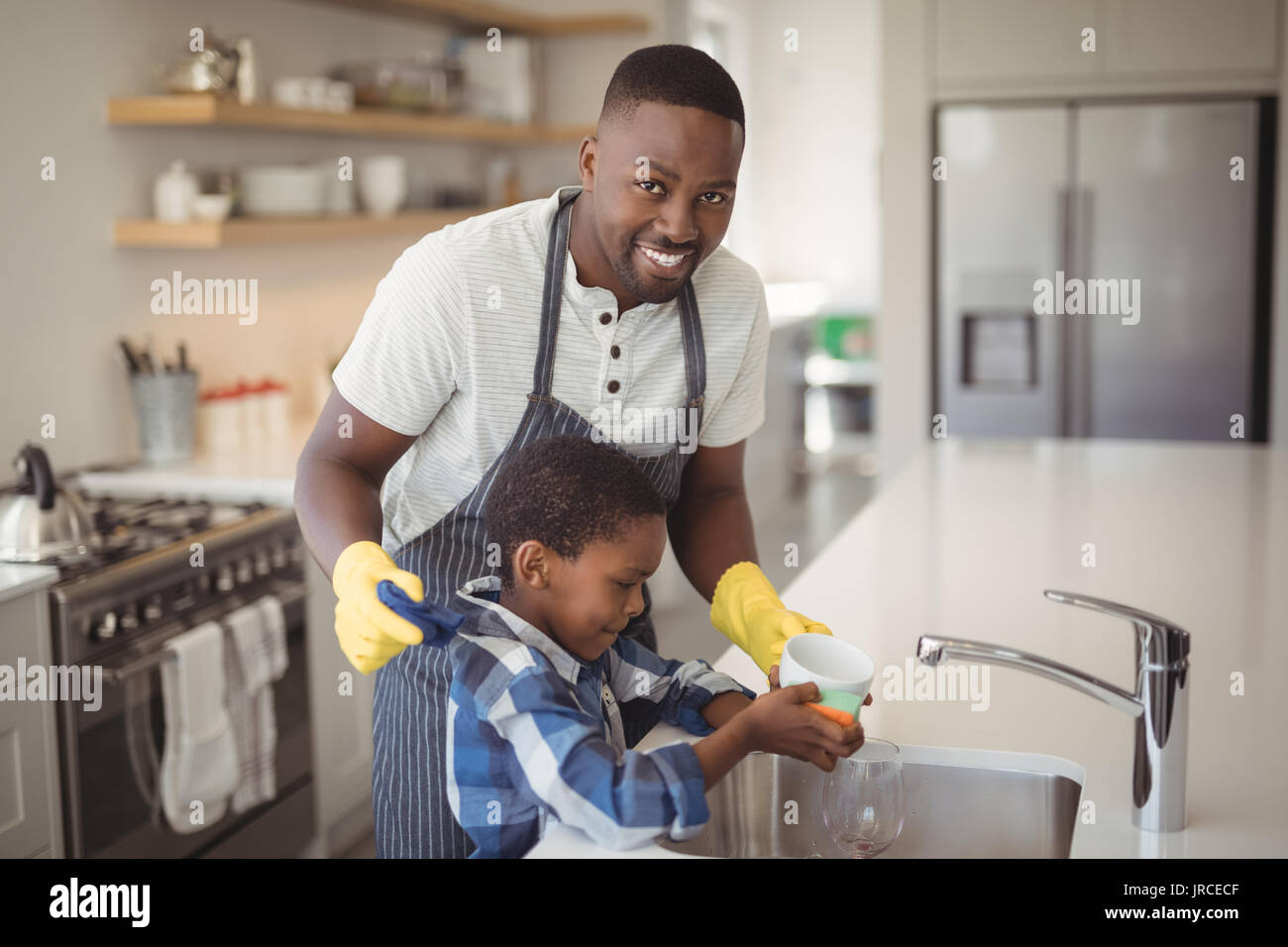 Portrait of smiling father and son cleaning cup in kitchen at home ...