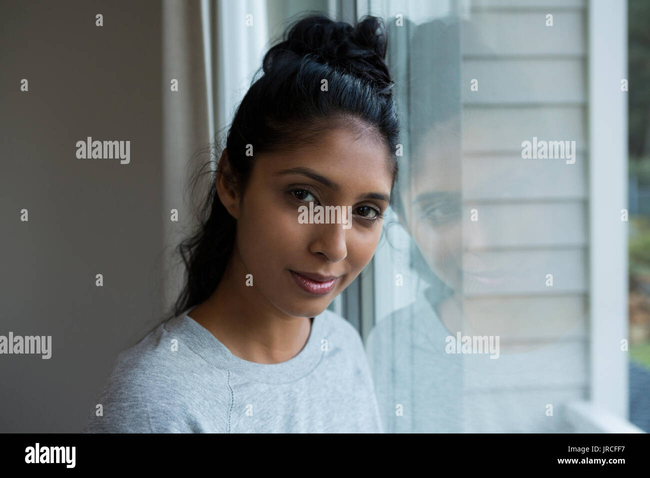 Portrait of young woman by glass window at home Stock Photo - Alamy